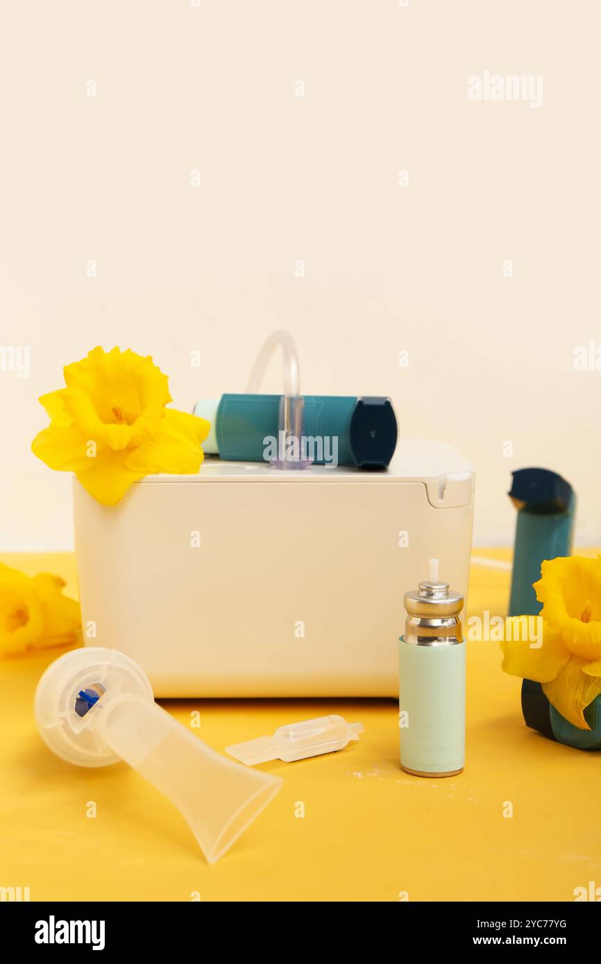 Modern nebulizer with inhalers and daffodil flowers on yellow table ...