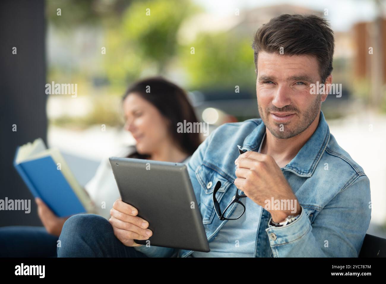 people at bus stop looking at book and tablet Stock Photo - Alamy