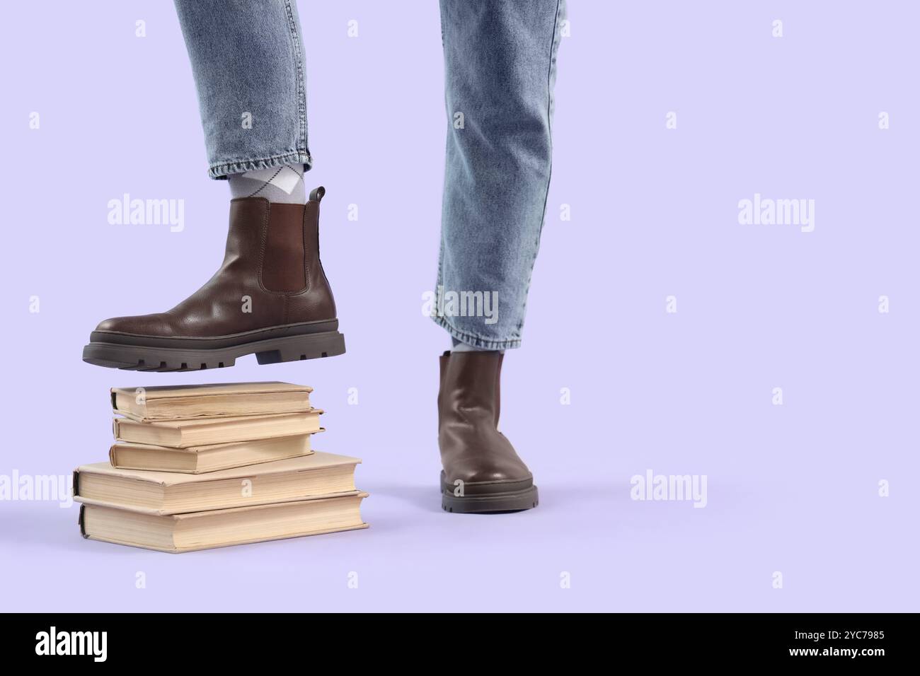 Young man in boots with stack of books on lilac background Stock Photo ...