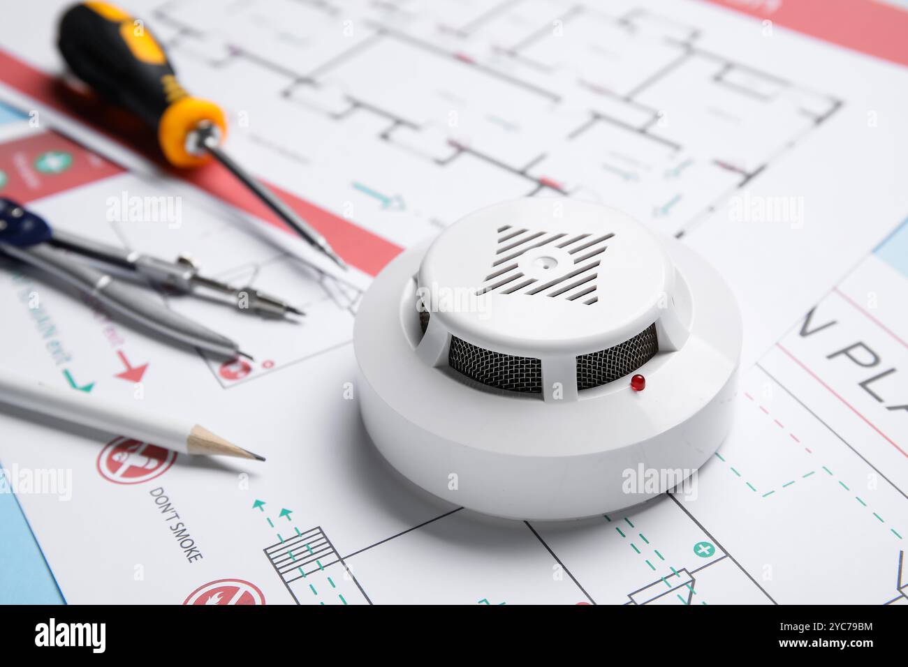 Modern smoke detector with supplies on evacuation plans, closeup Stock ...