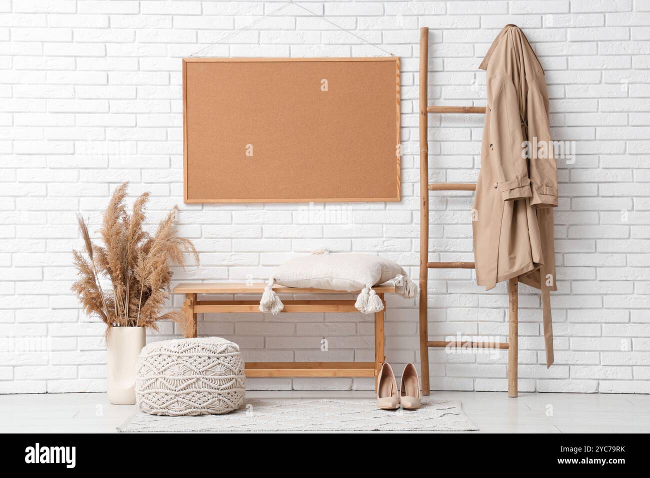 Bench, pouf and ladder with trench coat near white brick wall in room ...