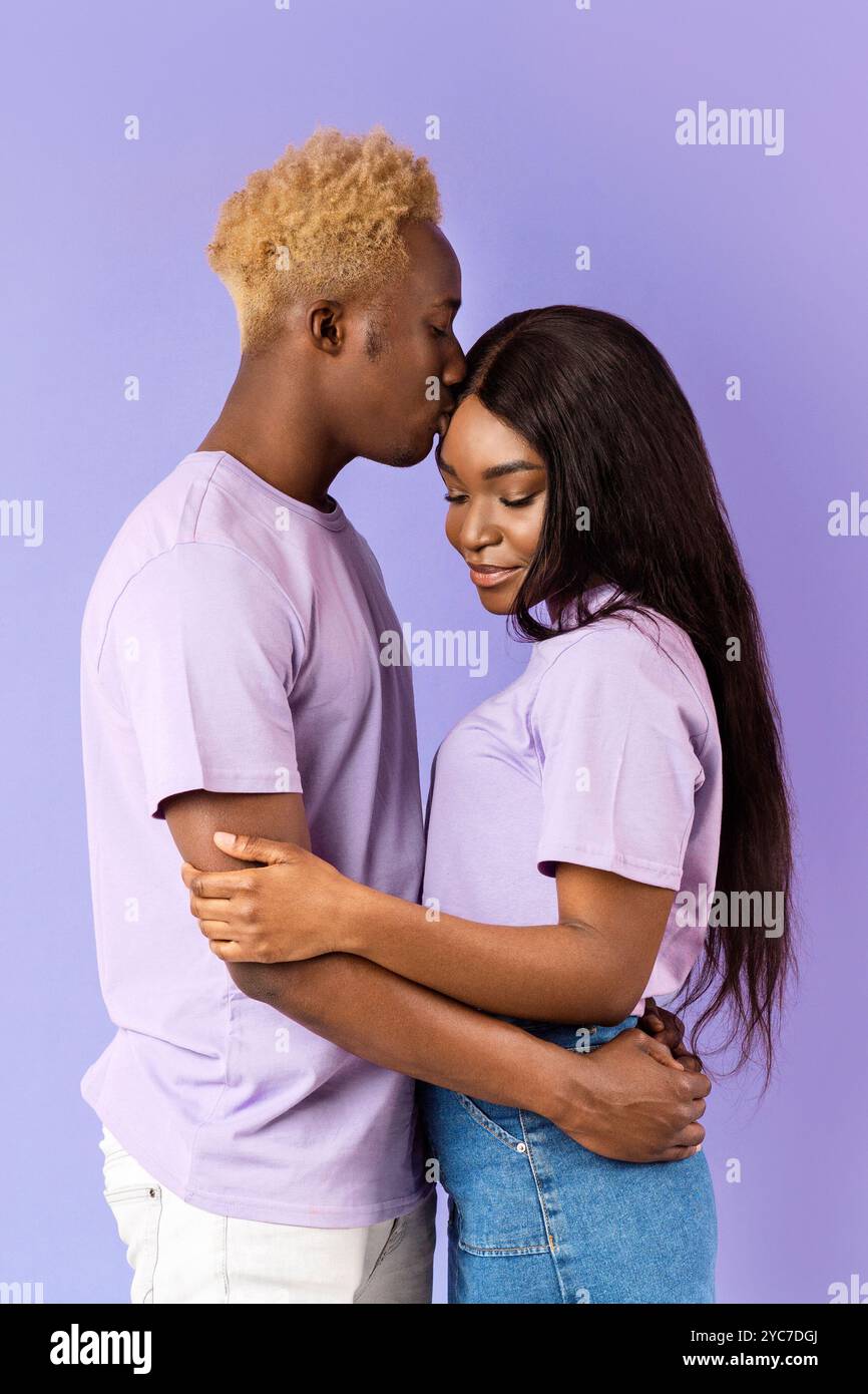 Millennial black guy hugging and kissing his girlfriend on lilac ...