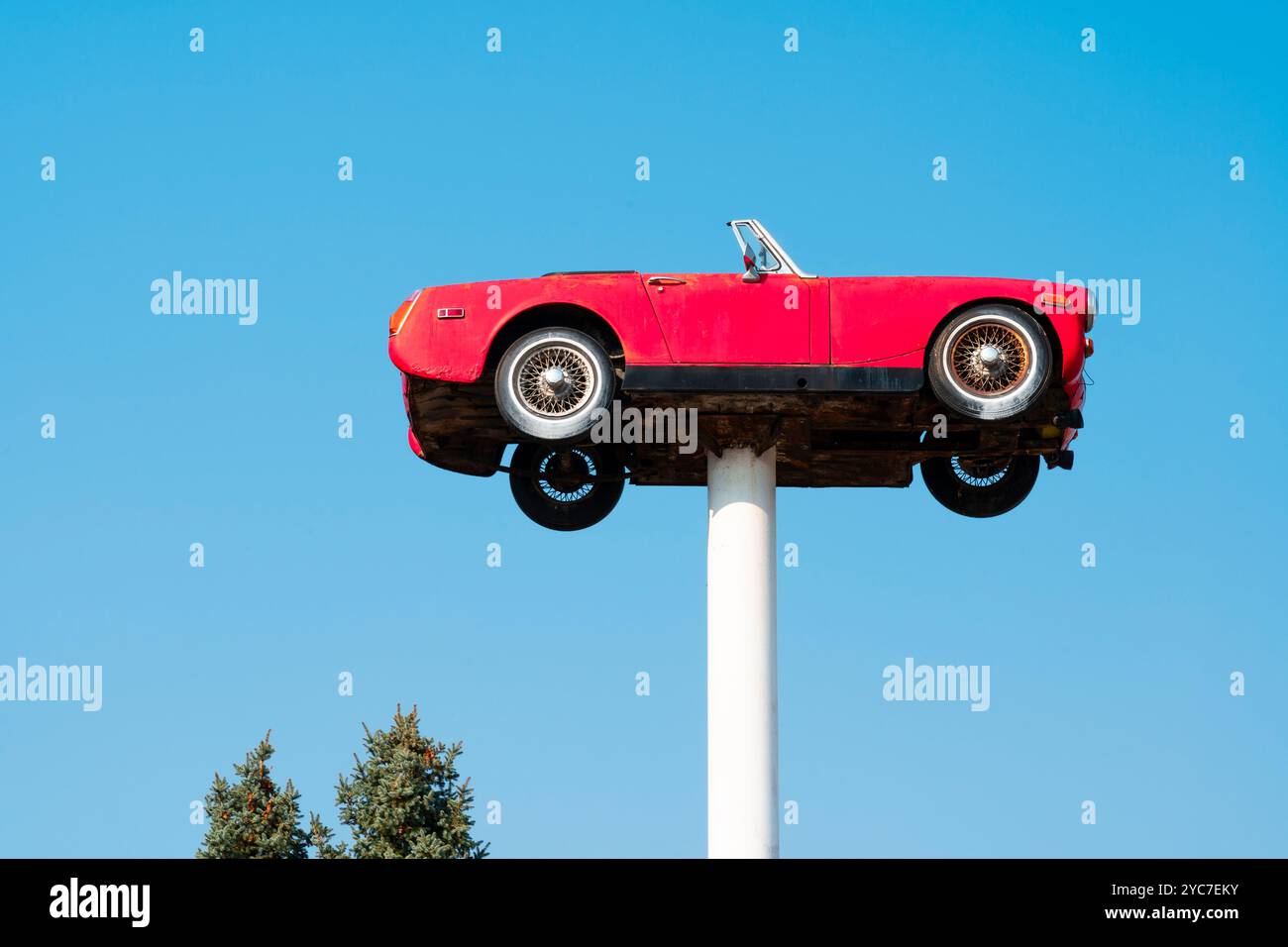Old automobile red sports car convertible is placed on a pole up in the ...