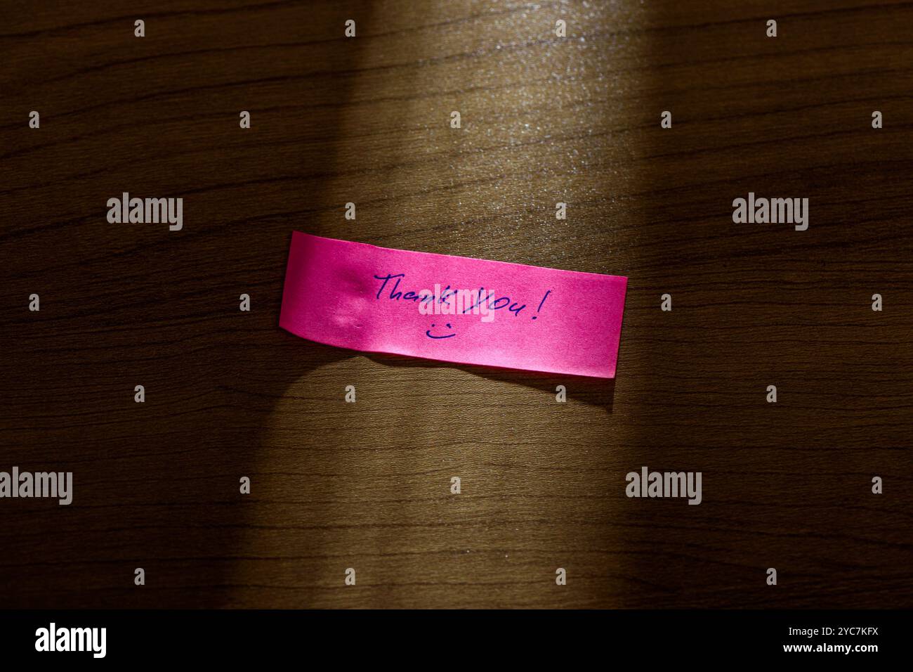 A pink sticky note with a handwritten Thank You on a wooden background ...