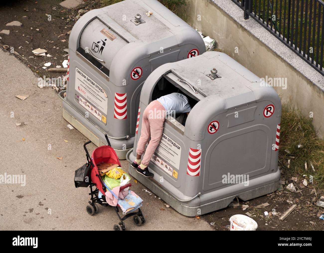 Young gypsy woman diving into garbage domestic waste bin checking for ...