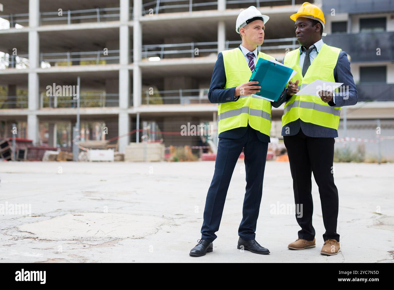 Two civil engineers are discussing the construction plan, holding ...