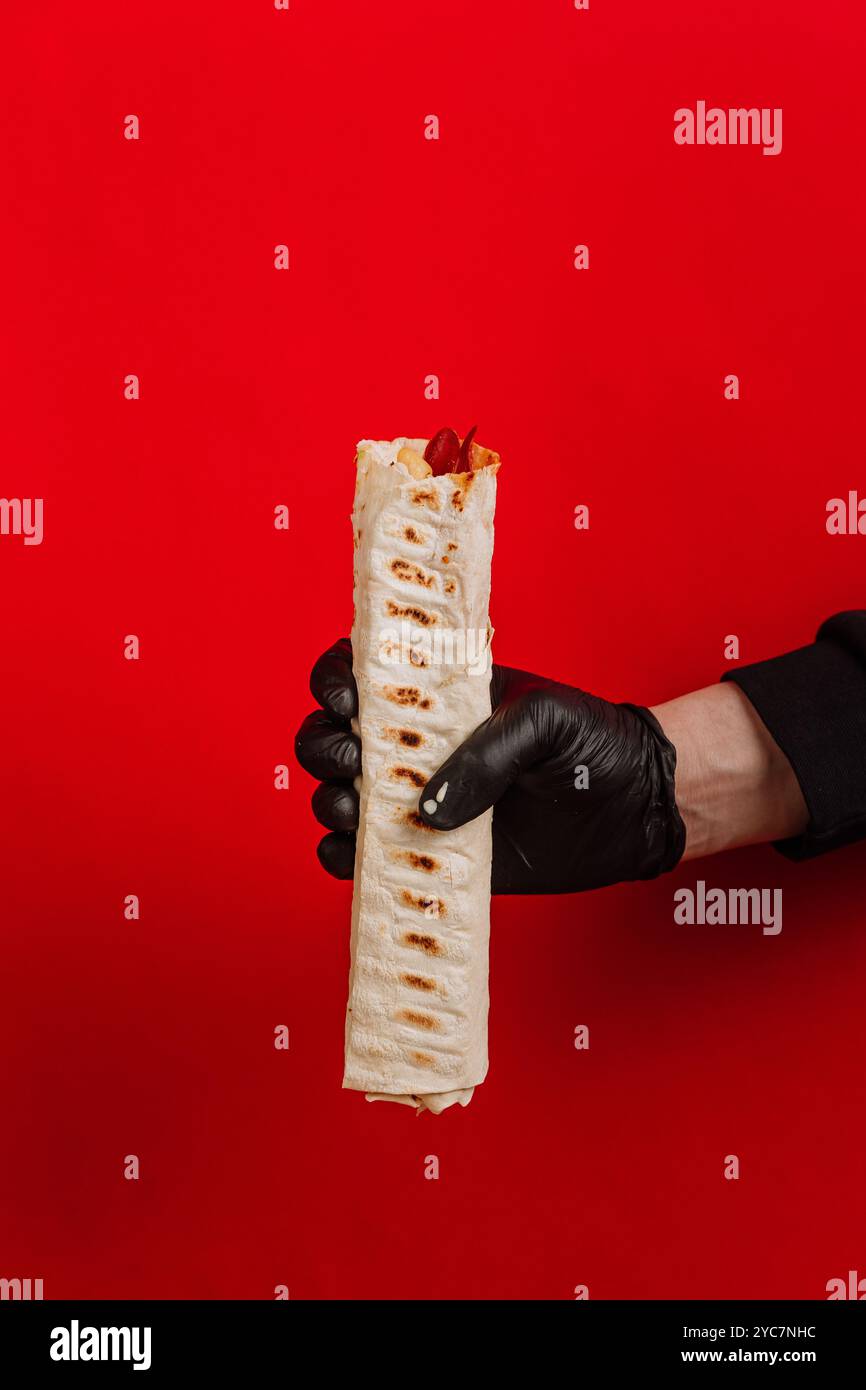 Hand holding wrap in paper against red background, fast food branding ...