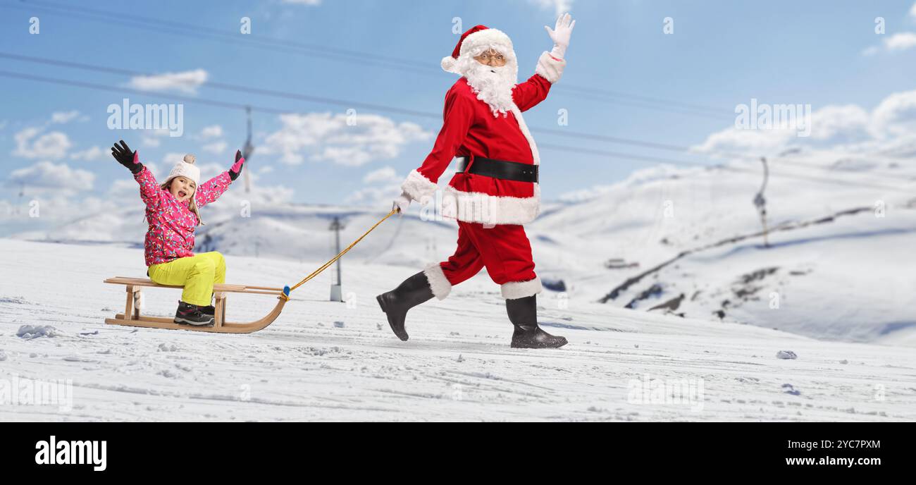Santa Claus waving and pulling a girl with a sled on a snowy hill Stock ...