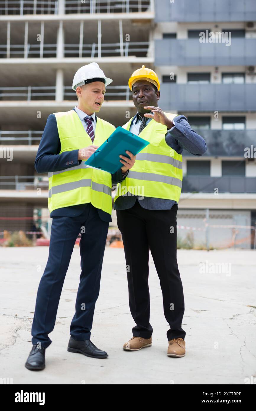 Two civil engineers are discussing the construction plan, holding ...