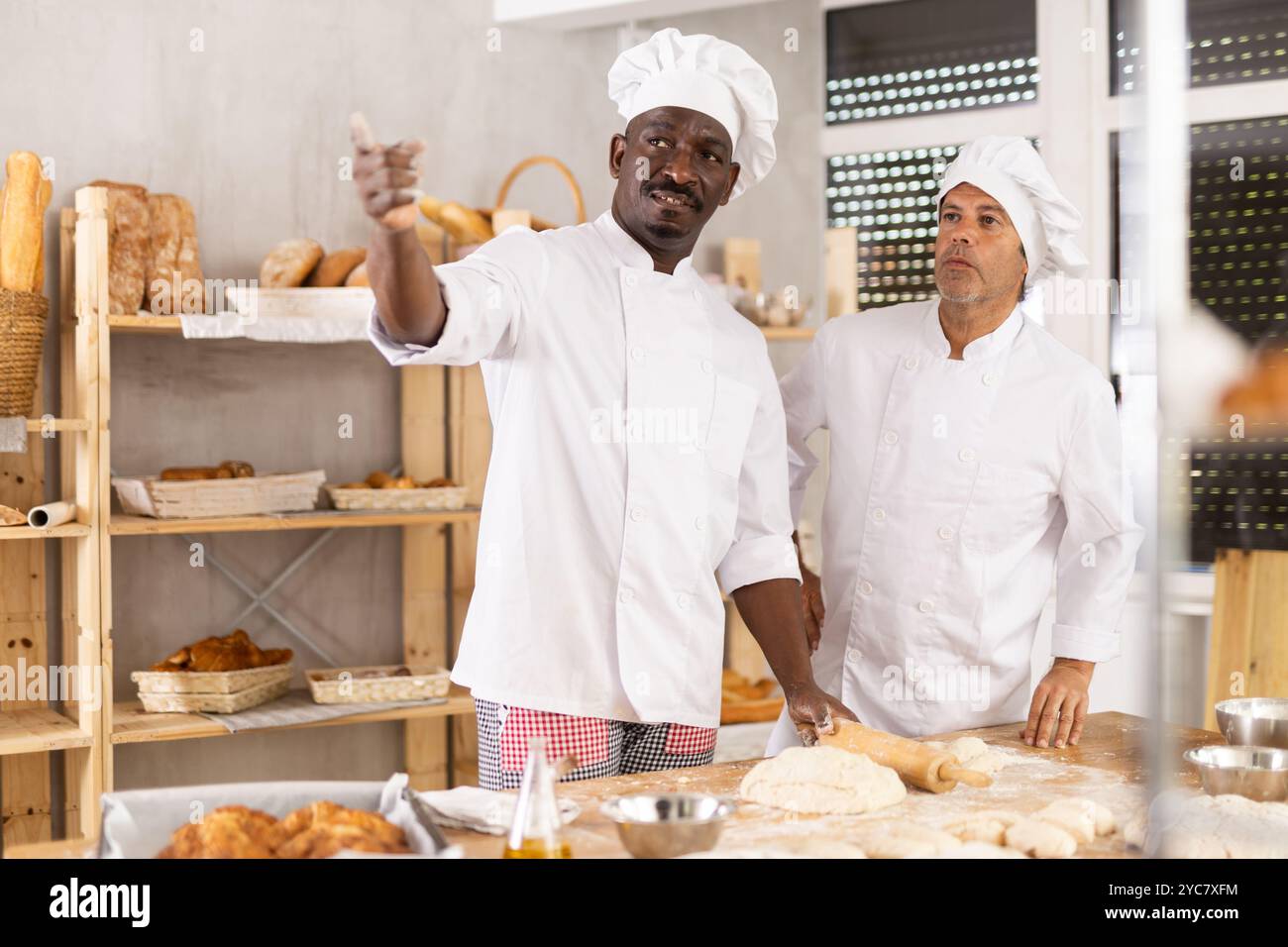 Master cook and his apprentice assistant are talking in bakery kitchen ...