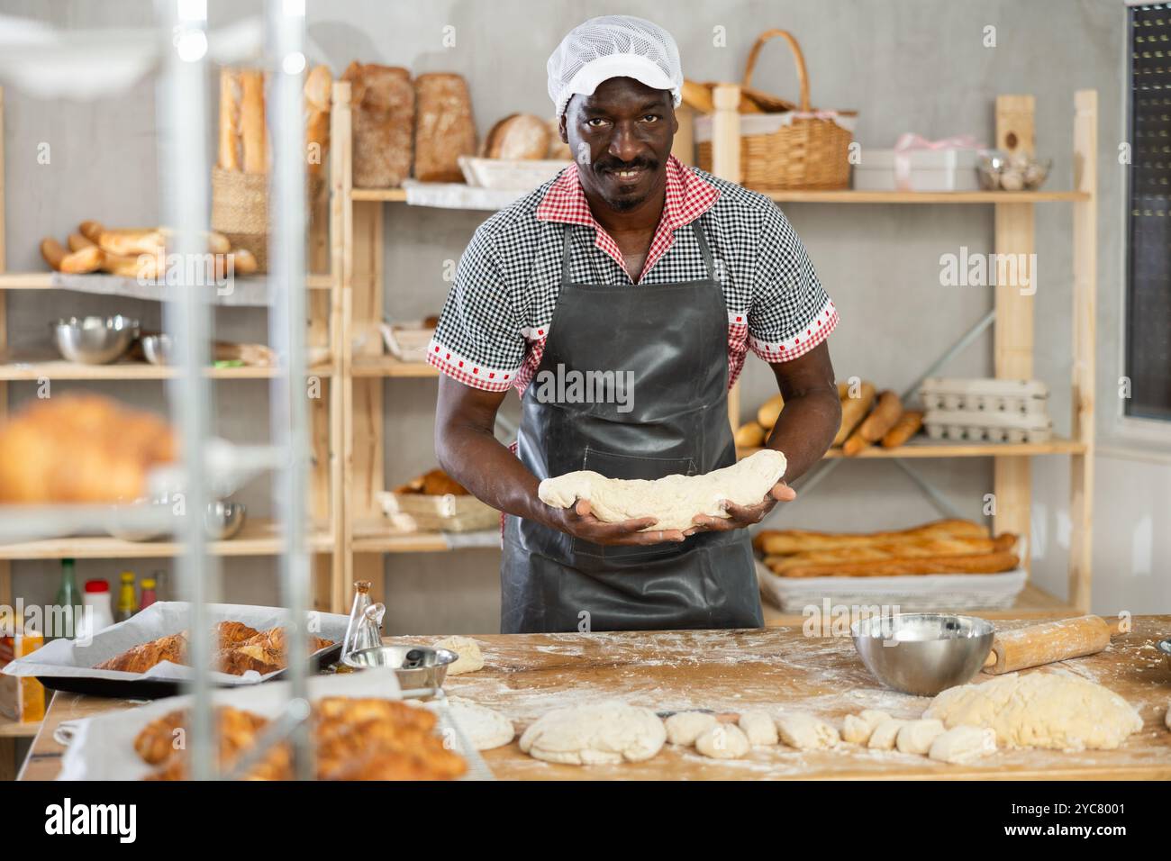 Professional male baker prepares raw yeast dough in bakery, shaping it ...