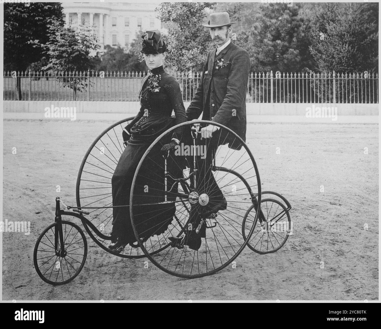 Smartly dressed couple seated on an late 19th century model bicycle for ...