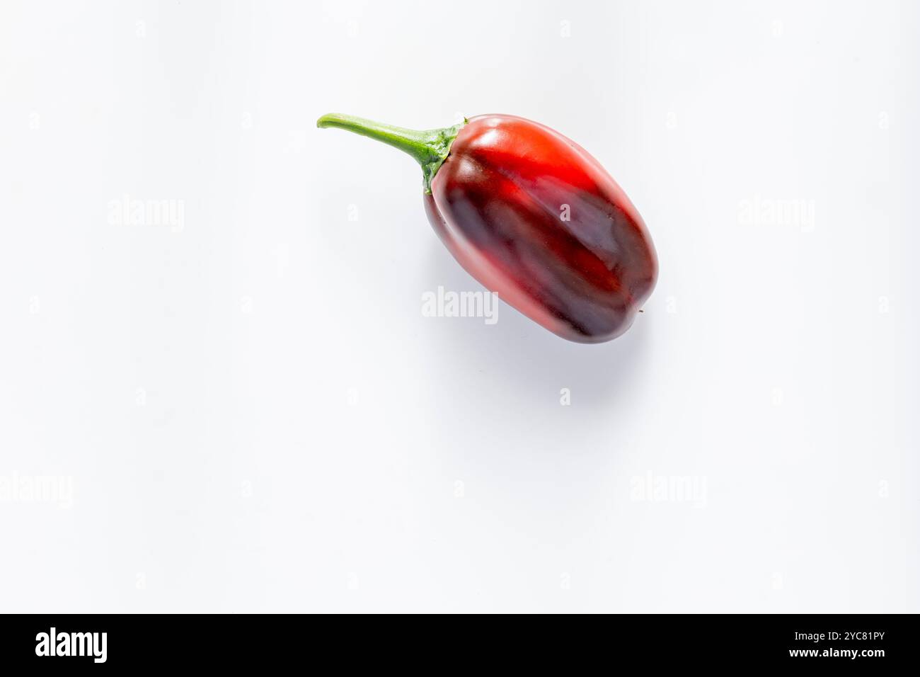 A single, ripe red bell pepper is positioned on a white background, its ...