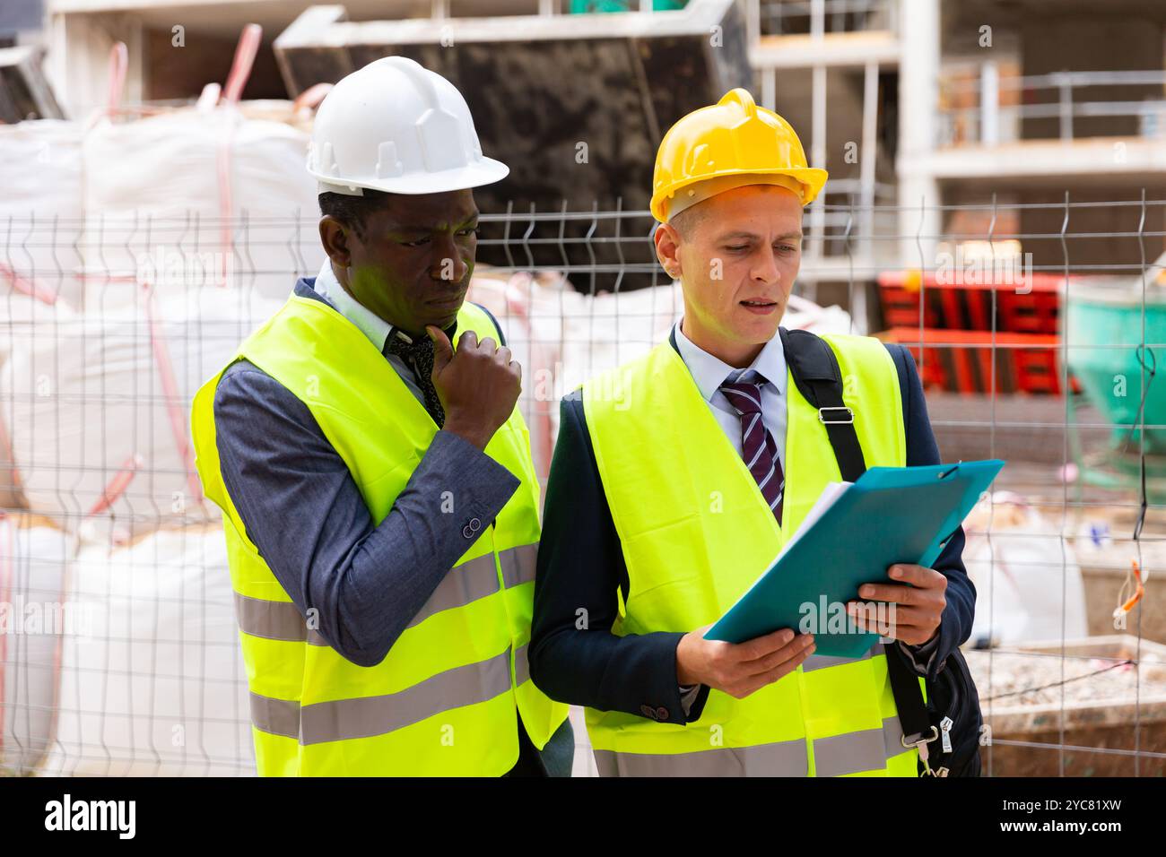 Two civil engineers are discussing the construction plan, holding ...