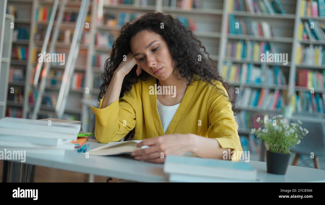 Tired Latino arabian woman sitting reading book studying knowledge exam ...