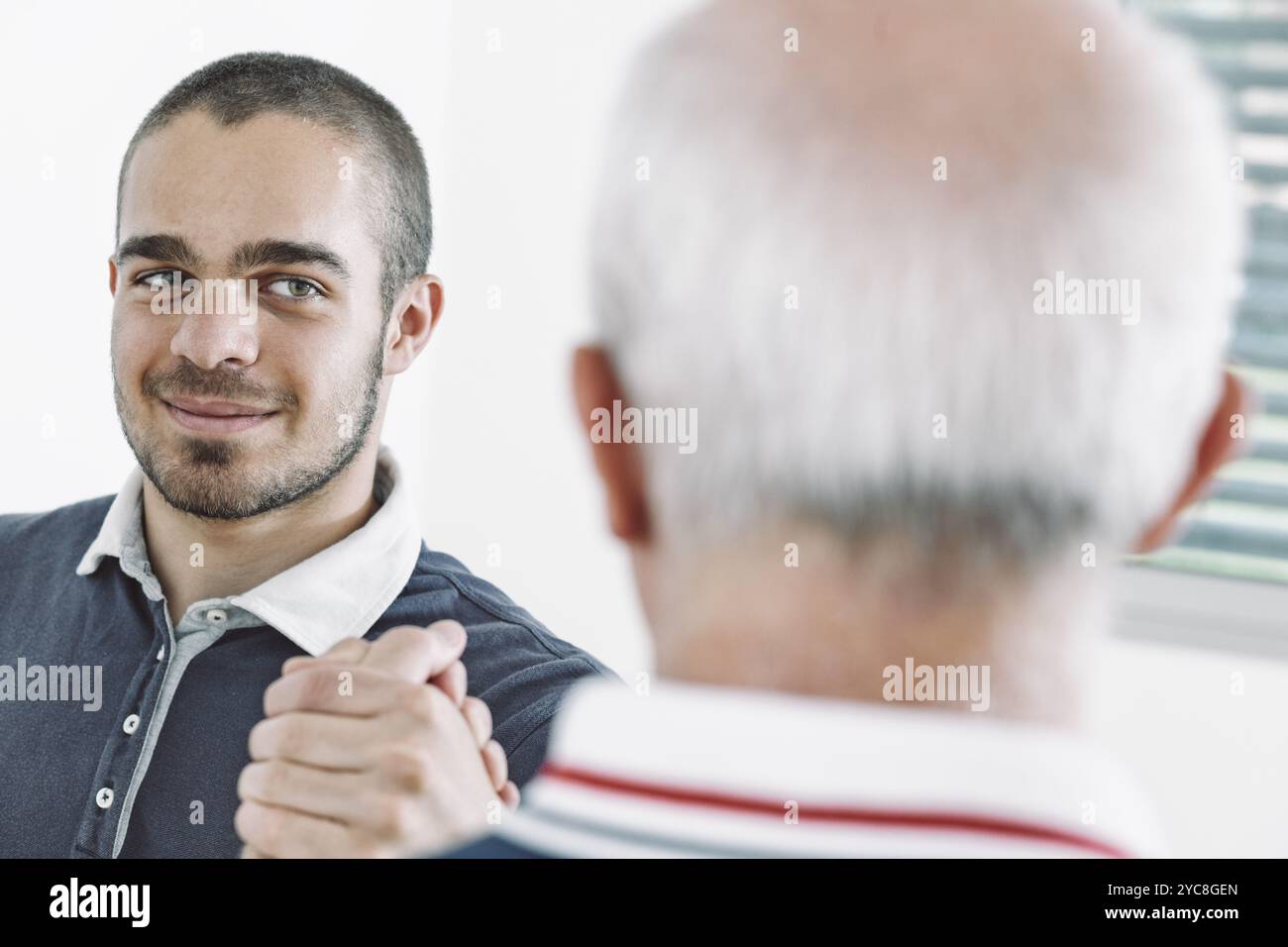 Young man and an older colleague shake hands in a bright office ...