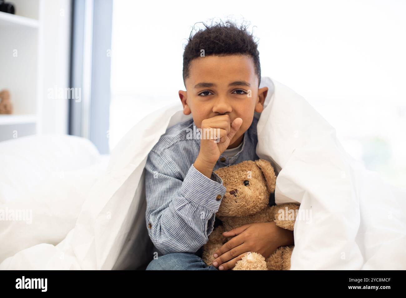 Sick boy sitting in bed cuddling teddy bear and coughing Stock Photo ...