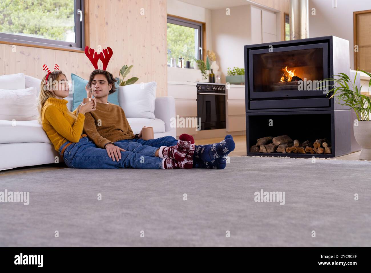 Christmas time, in festive antlers, couple relaxing by fireplace in ...
