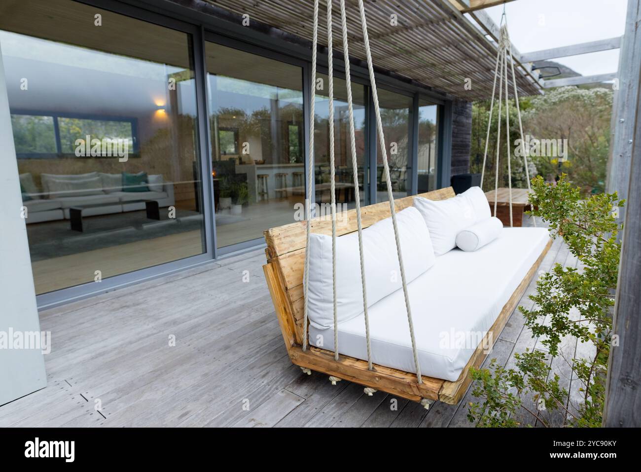 Wooden swing sofa on modern patio with glass doors and lush greenery ...