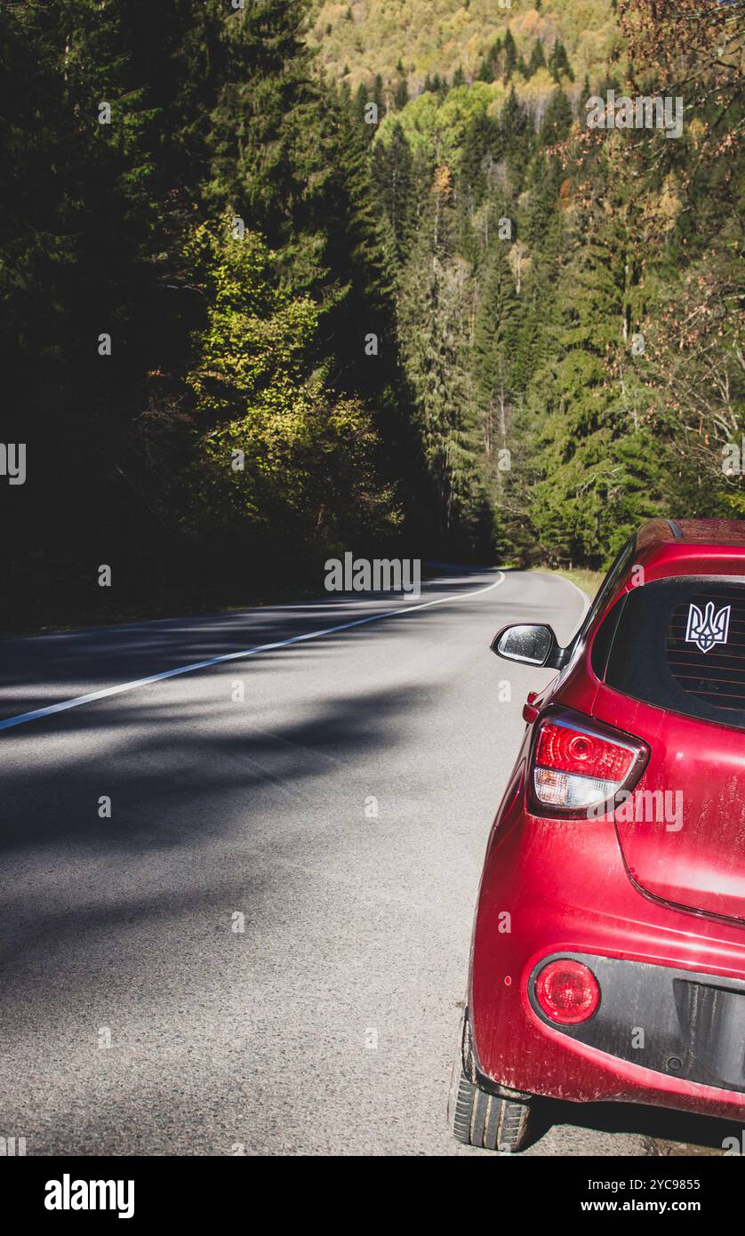 Red car with Ukrainian trident symbol on curved road in the mountains ...
