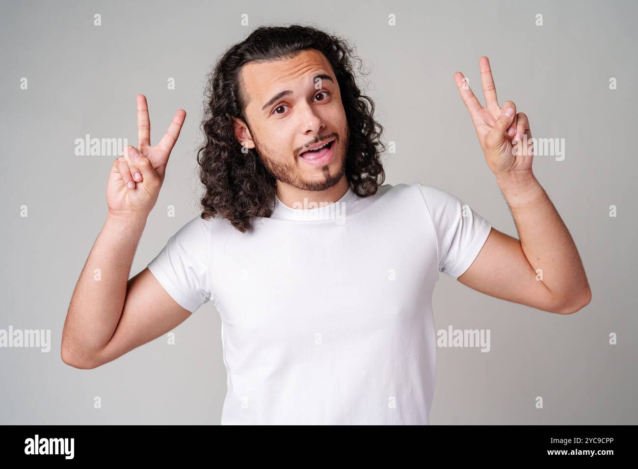 Young man with curly hair playfully posing with peace signs against a ...