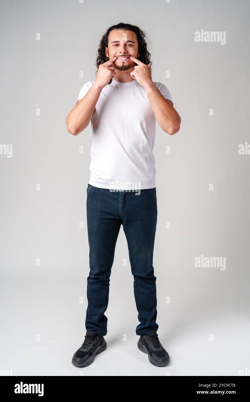 Young man in a white t-shirt playfully smiles while pointing to his ...