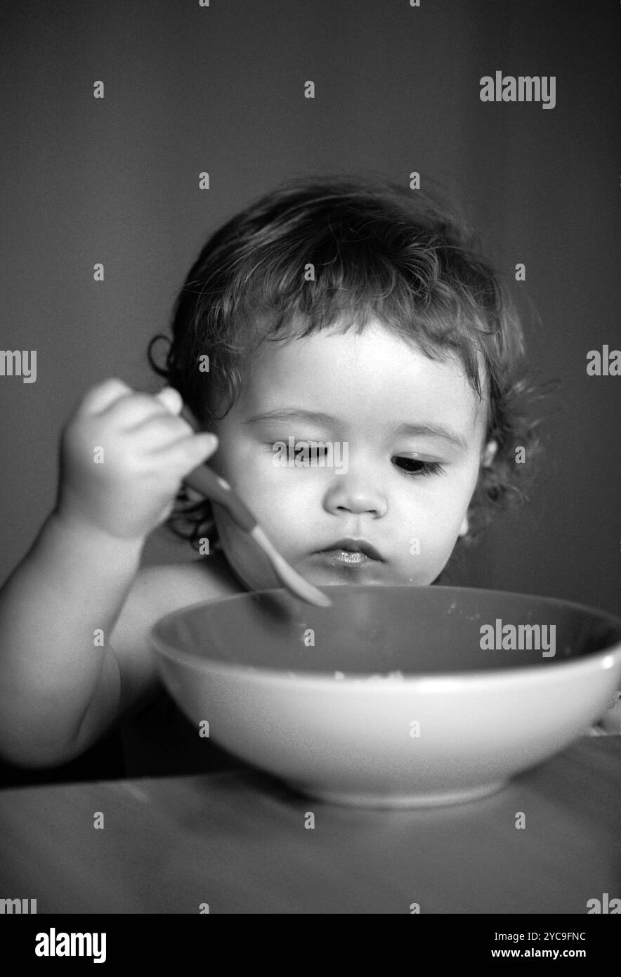 Child nutrition concept. Funny baby eating food himself with a spoon on ...