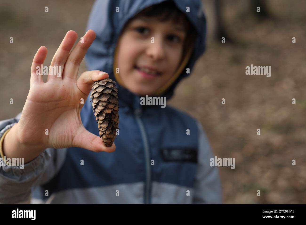 Child in a blue jacket holding pine cones over his eyes, smiling ...