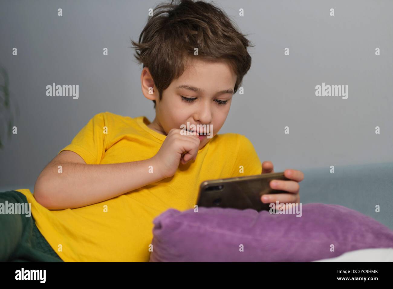 Little asian boy playing on the phone and chewing on his feet, the ...