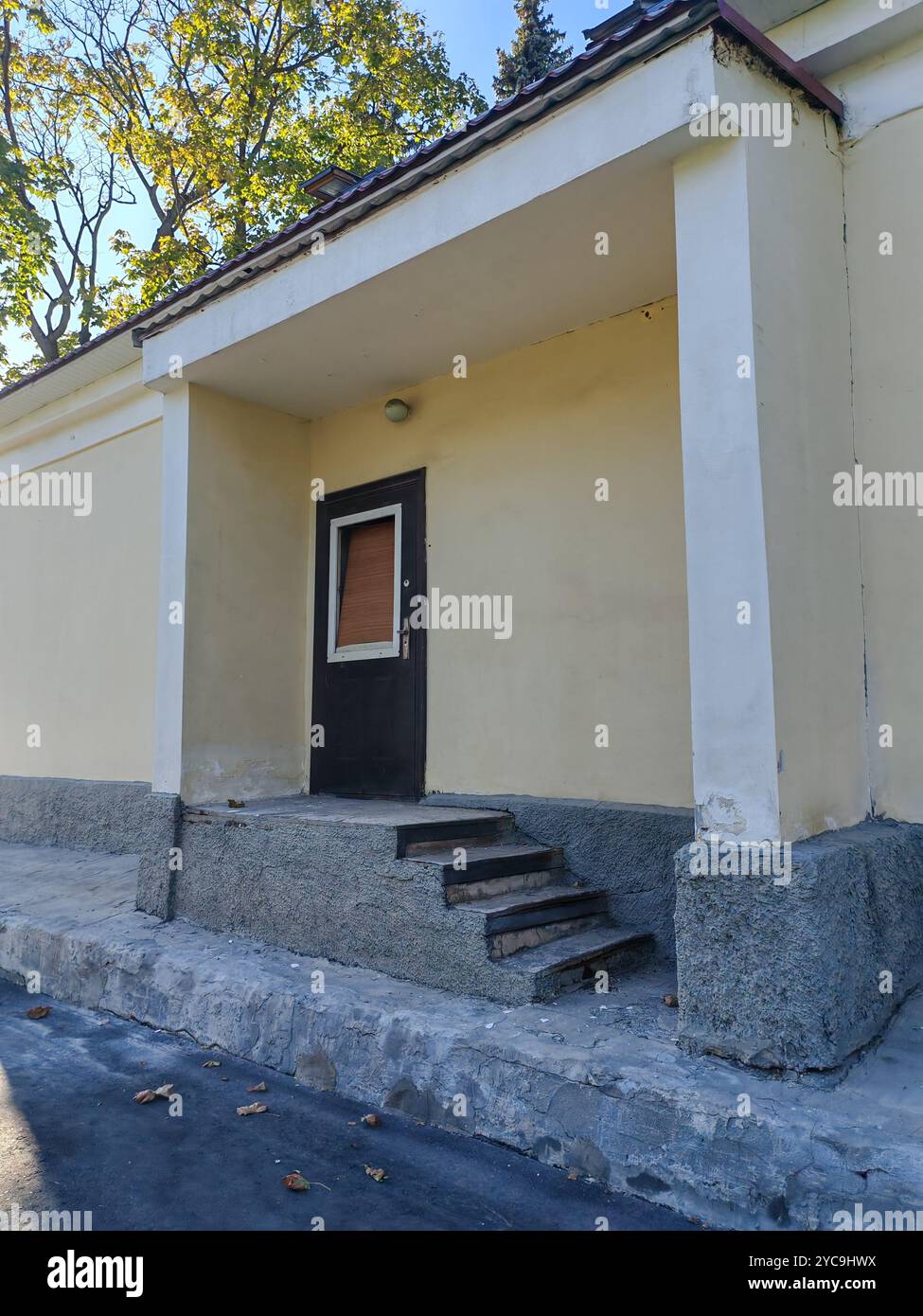 A small entrance with concrete steps leading to a dark wooden door ...