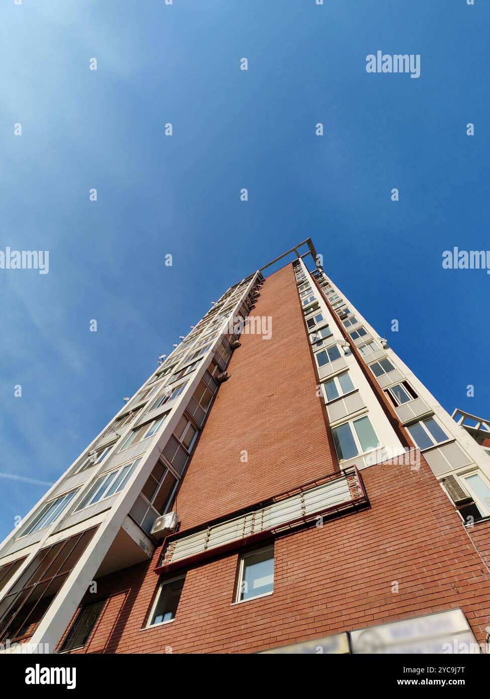 A tall red and beige brick residential building with multiple balconies ...
