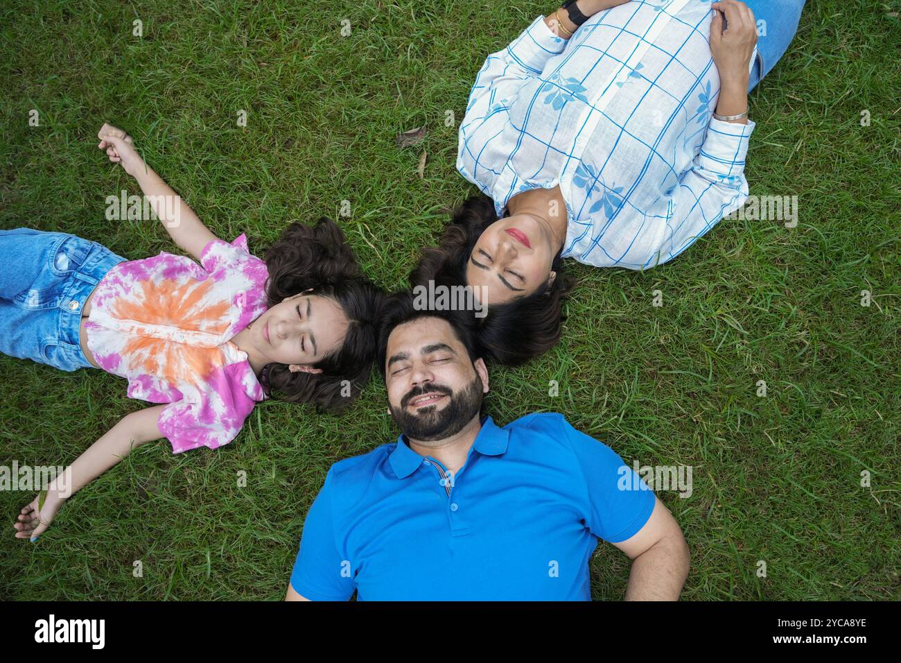 Top view of happy young indian family of three lying on grass in circle ...