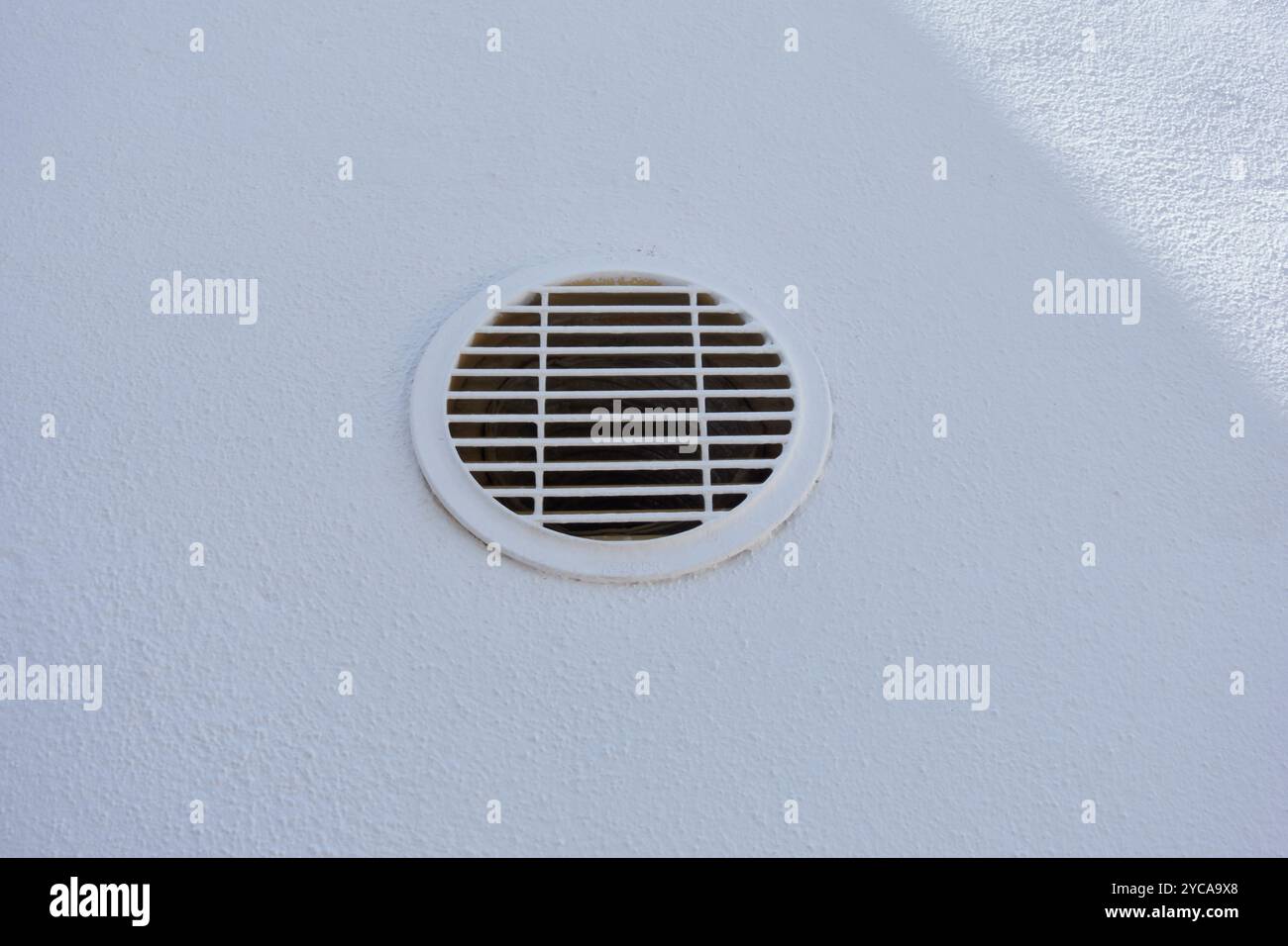 A circular white plastic air vent with horizontal slats on a textured ...