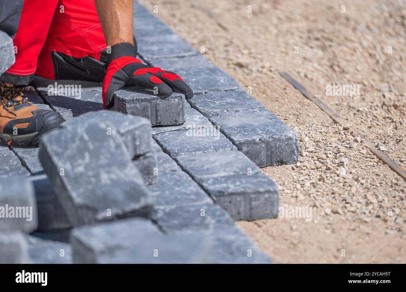 A construction worker is carefully placing grey pavers on a prepared ...