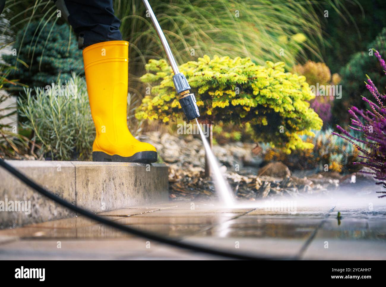 A person is using a pressure washer to clean a patio surface while ...
