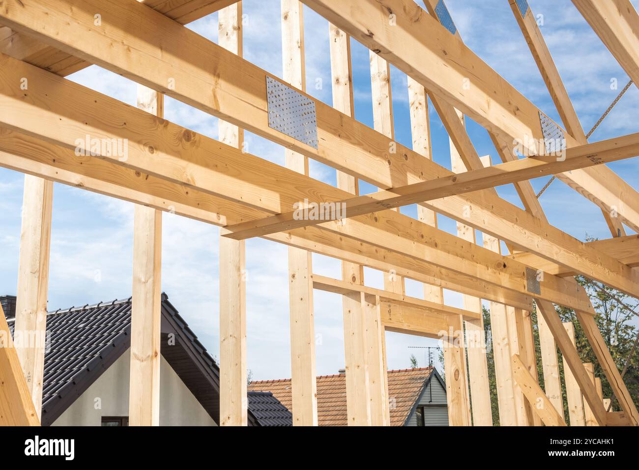 Workers are building the framework of a house, showcasing the wooden beams and trusses against a ...