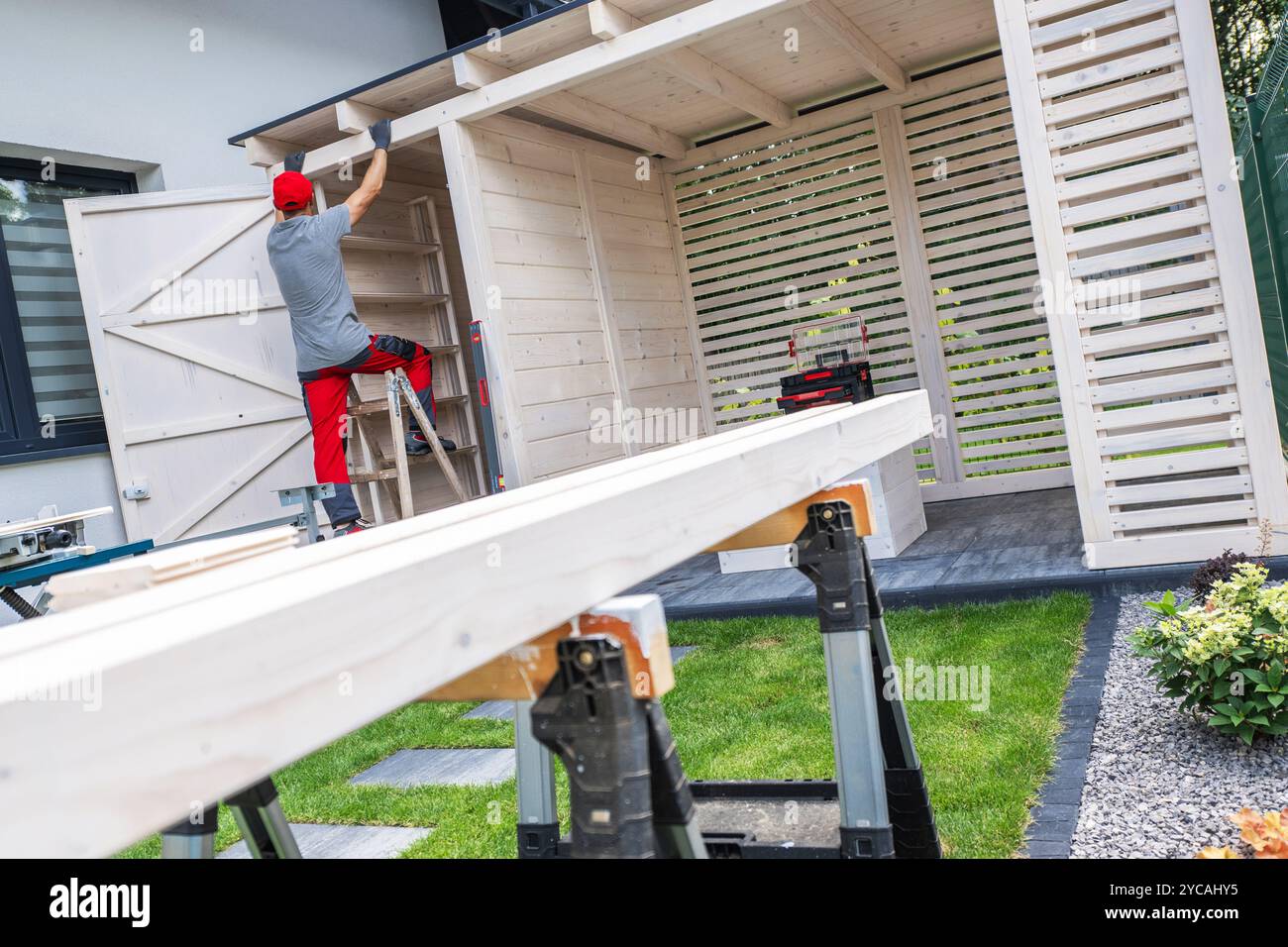 A skilled worker is constructing a wooden shed in a backyard, using a ...