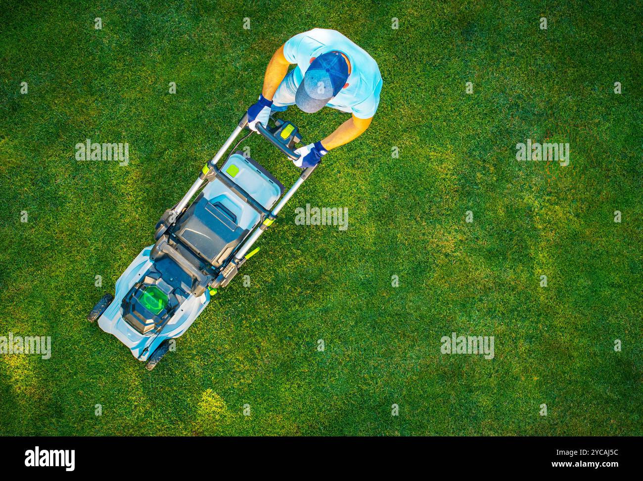 Under bright sunlight, a person mows a well-maintained lawn using a ...