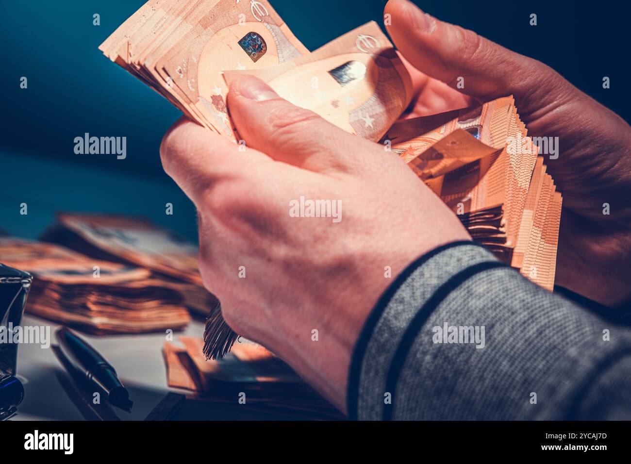 A person is counting stacks of Euro banknotes in a softly lit room ...