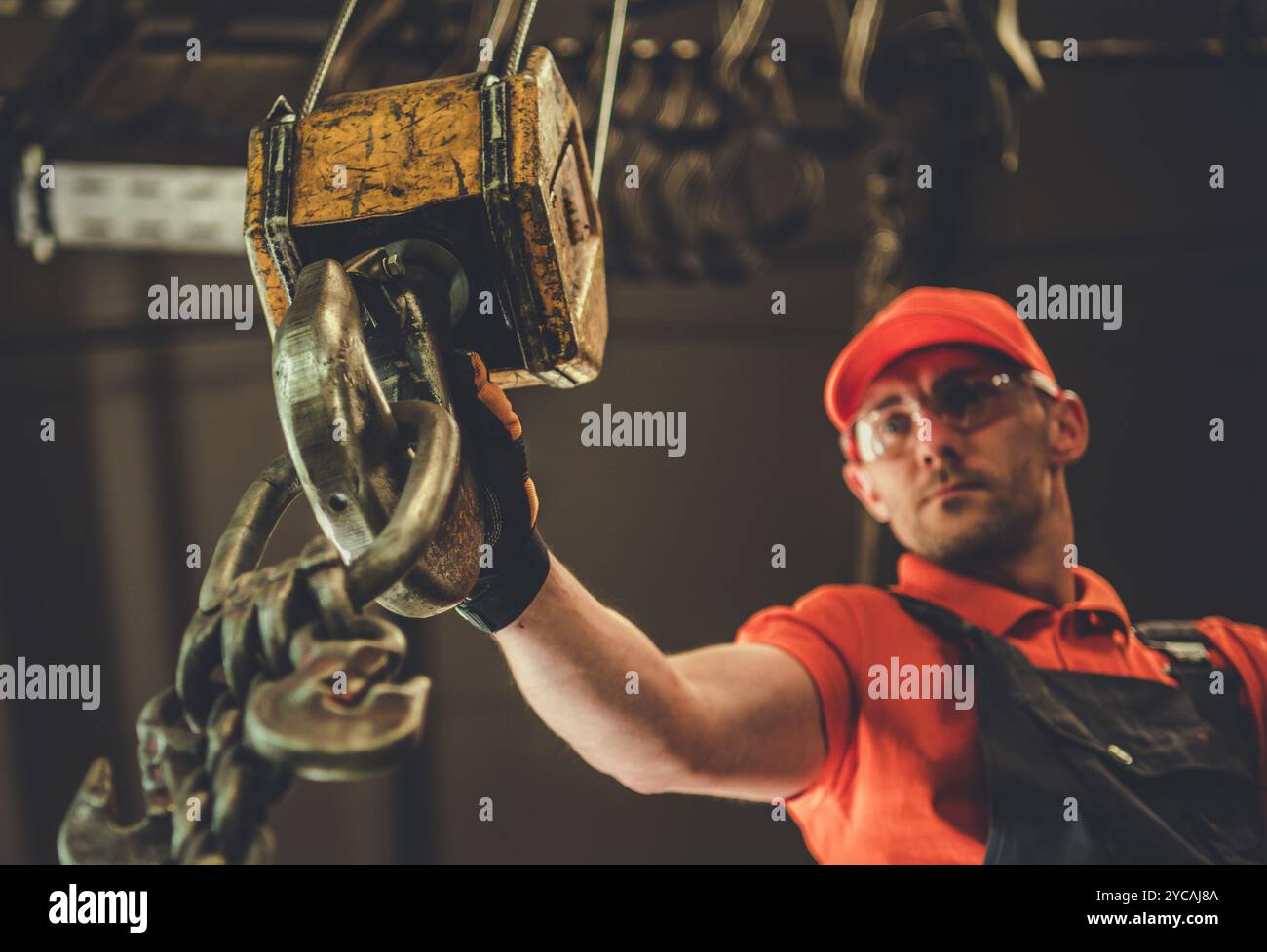 A skilled worker in safety gear maneuvers a crane hoist, lifting heavy ...