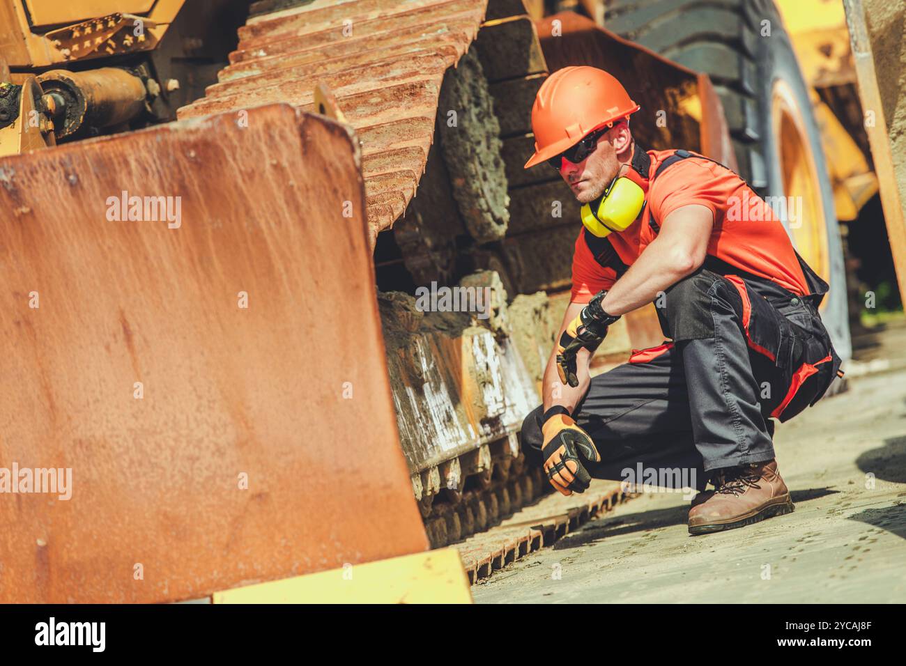 A construction worker in an orange shirt and helmet inspects heavy ...