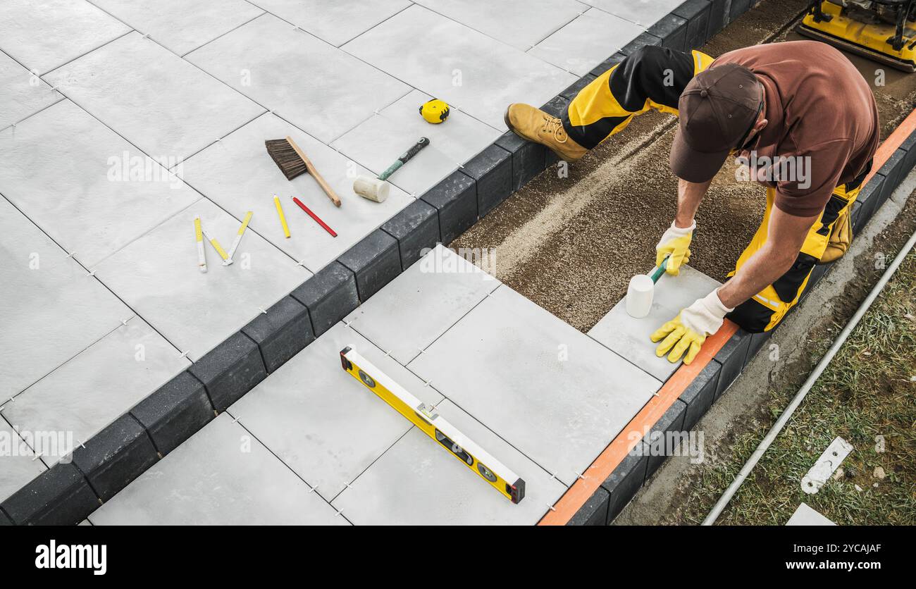 A skilled contractor is carefully positioning pavers in a backyard ...