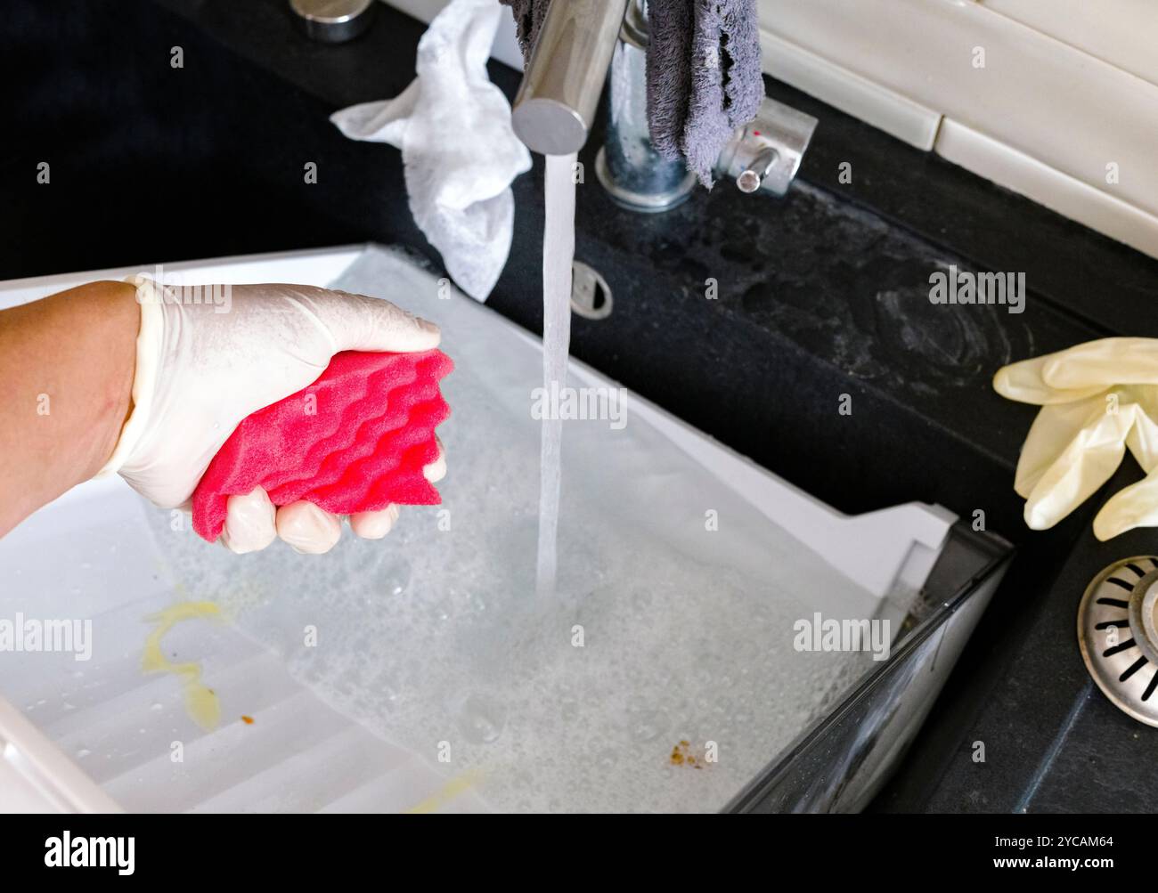 a hand is disposable glove washing plastic fridge box in a kitchen sink ...