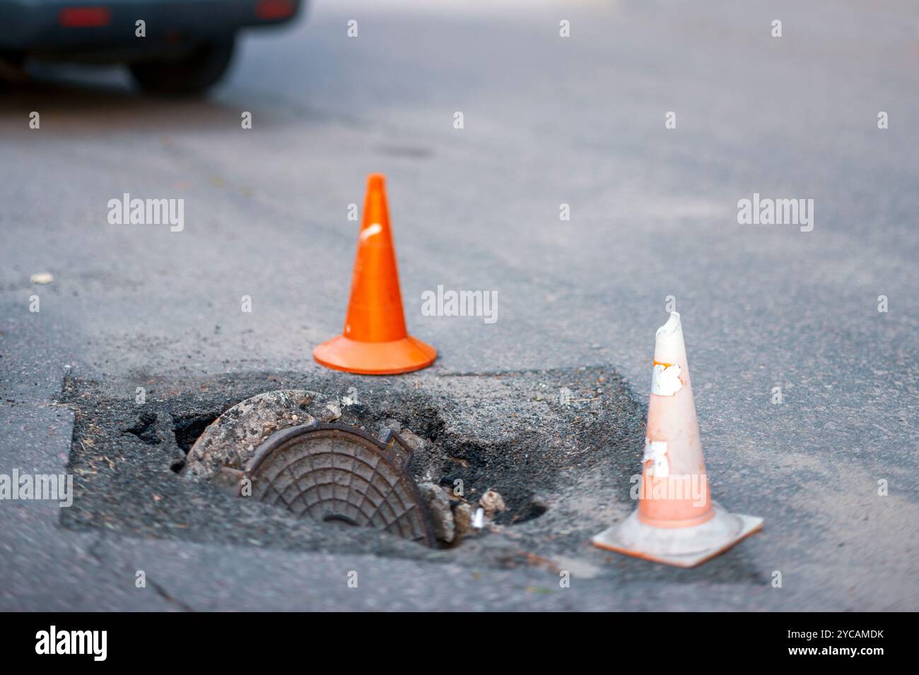 a damaged manhole with cast iron cover and cracked asphalt, outdoor ...