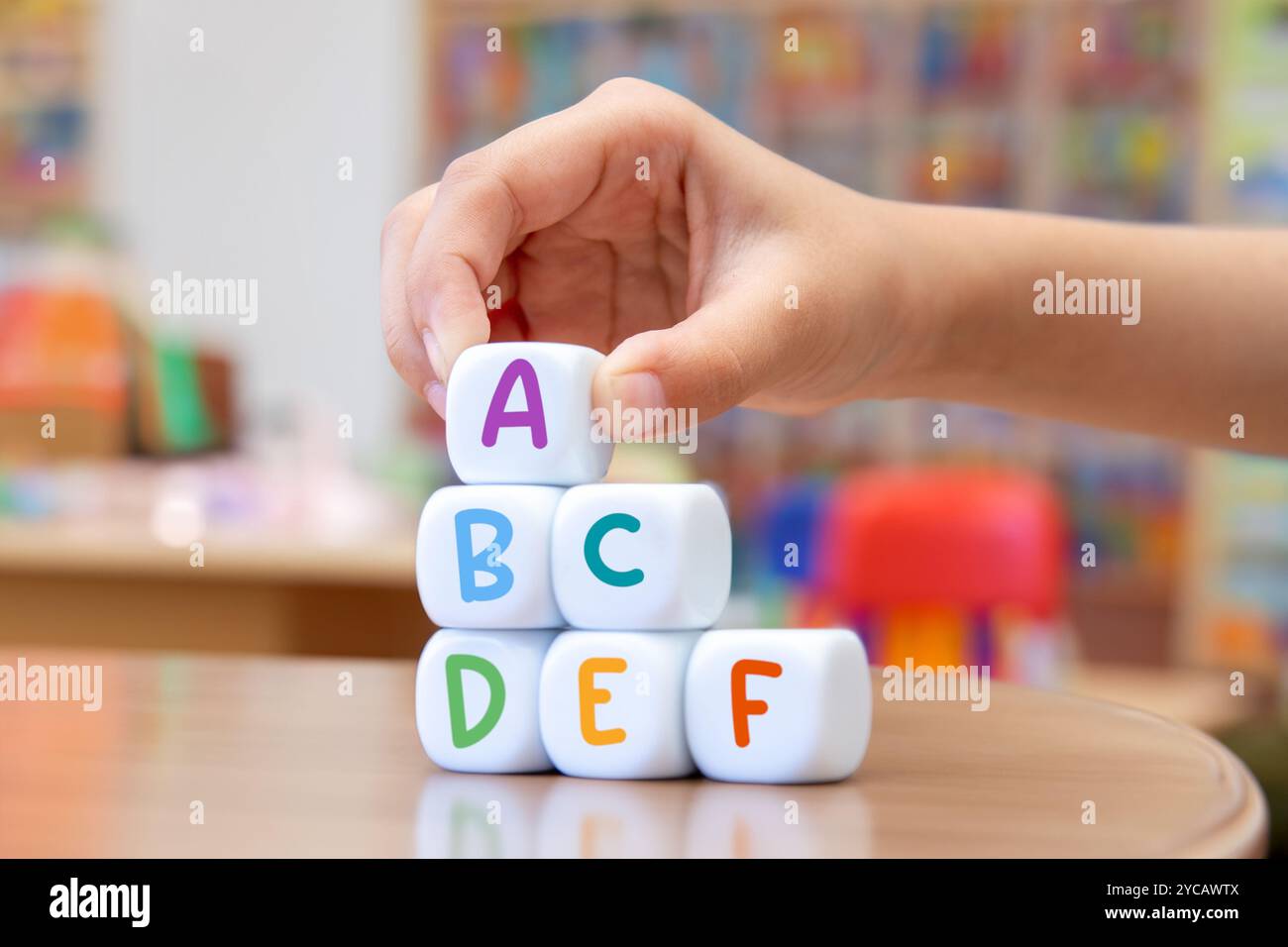 A child's hand playing with alphabet cube in classroom. Early childhood ...
