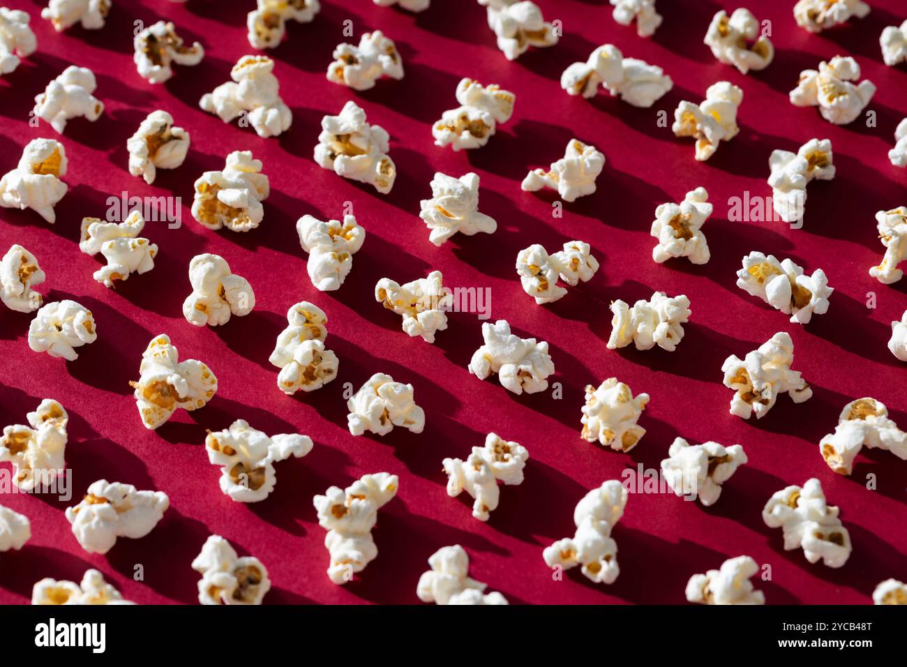Scattered popcorn pieces cast shadows on a vibrant red background ...