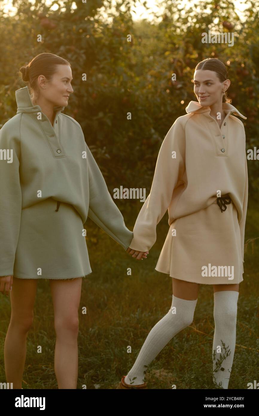 Two models in stylish tracksuits pose in apple orchard at sunset . The ...