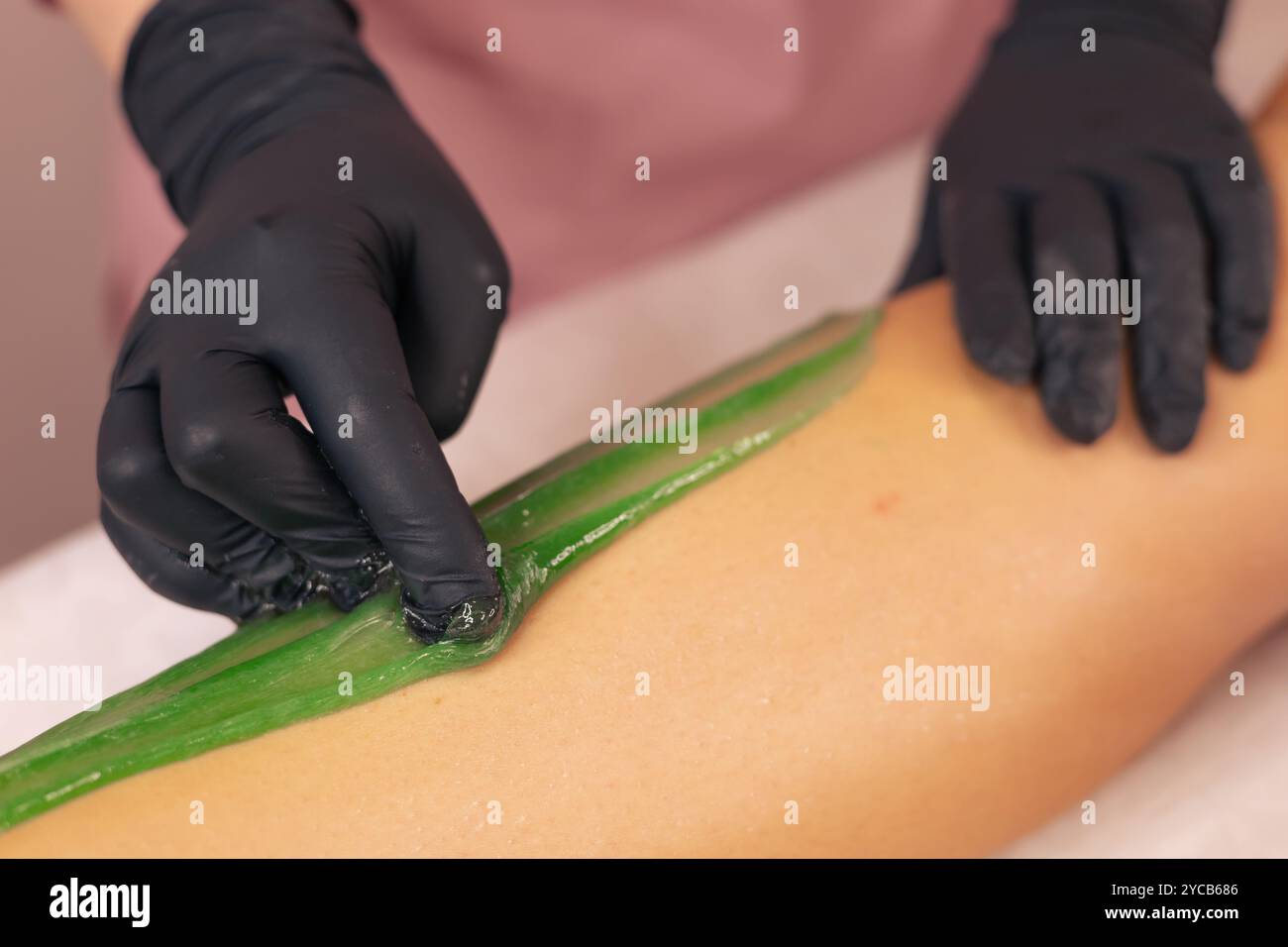 Aesthetician performing a green wax treatment on a clients leg in a spa ...
