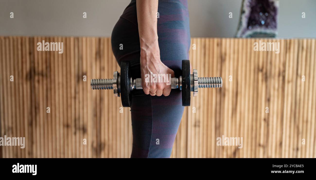 A person grips a dumbbell firmly in their right hand, showing toned forearm muscles, wearing ...