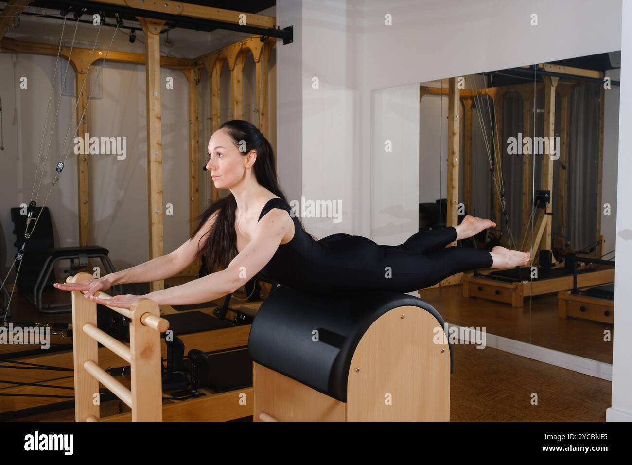 Young girl doing Pilates barre in a gym. Beautiful slim woman in black ...